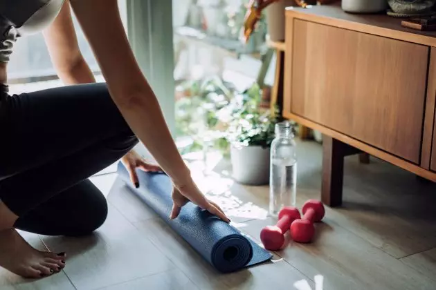 Paano gumawa ng home workout: Close up ng batang Asian sports woman na nagsasanay ng yoga / nag-eehersisyo sa bahay. Naglalahad ng yoga mat, naghahanda para mag-ehersisyo sa sariwang maliwanag na umaga