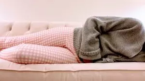 PMDD-ի ախտանշանները. մի կին պառկած է բազմոցին՝ ցավից բռնած ստամոքսը