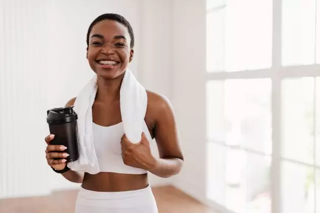 خواتین کے لیے بہترین پروٹین پاؤڈر: سفید کھیلوں کے لباس میں اسپورٹی خوبصورت مسکراتی ہوئی سیاہ فام عورت کا پورٹریٹ