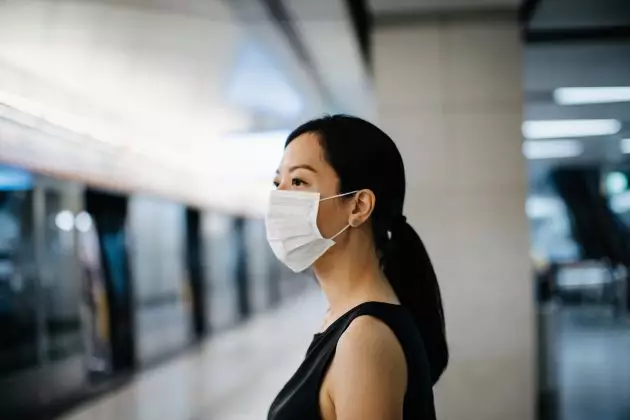 Keqinformimi i vaksinës: Gruaja aziatike me maskë mbrojtëse për fytyrën duke pritur trenin MTR të metrosë në platformë
